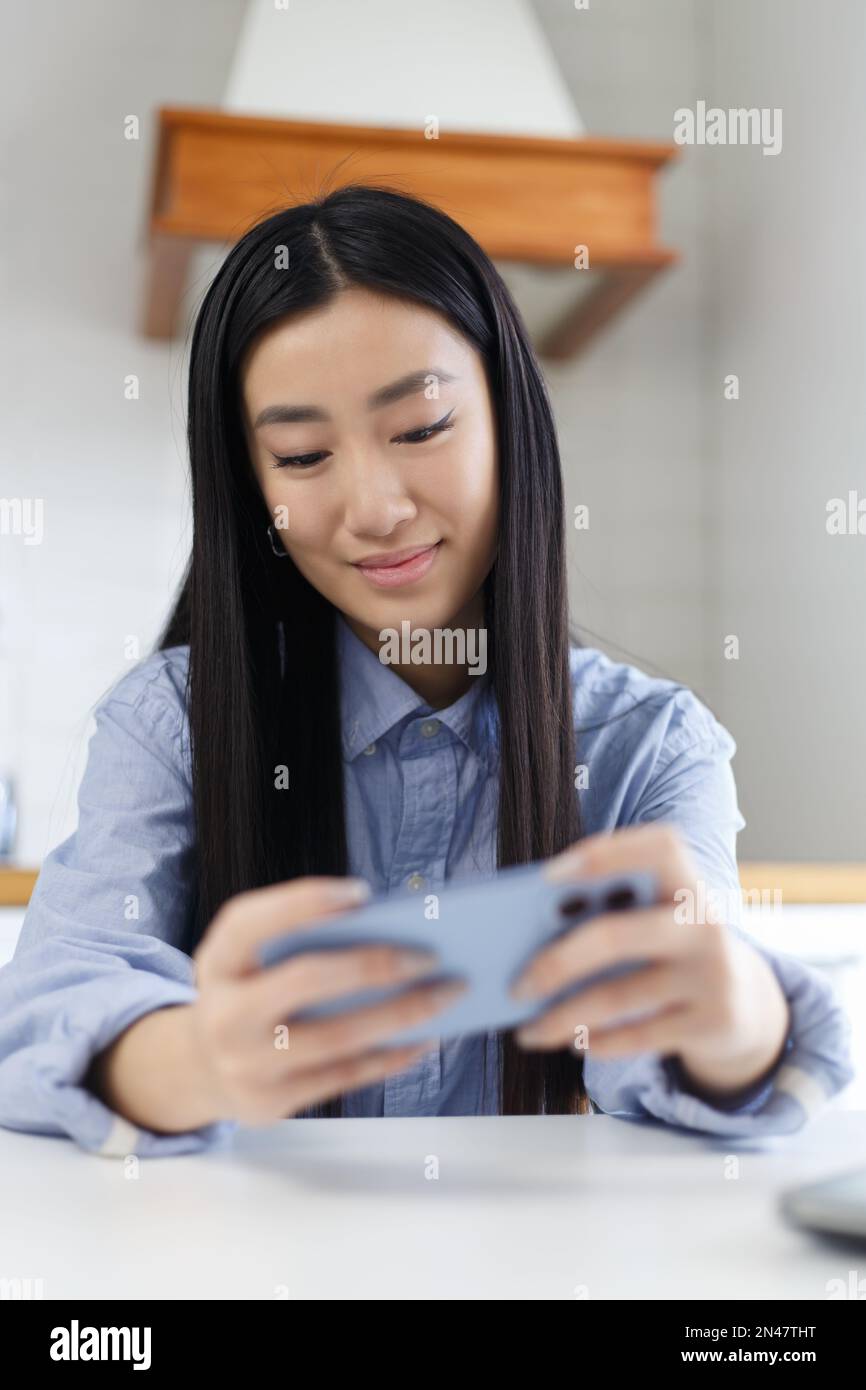 Beautiful Asian girl plays online game with a smart phone. Cheerful Vietnamese POC female using ...