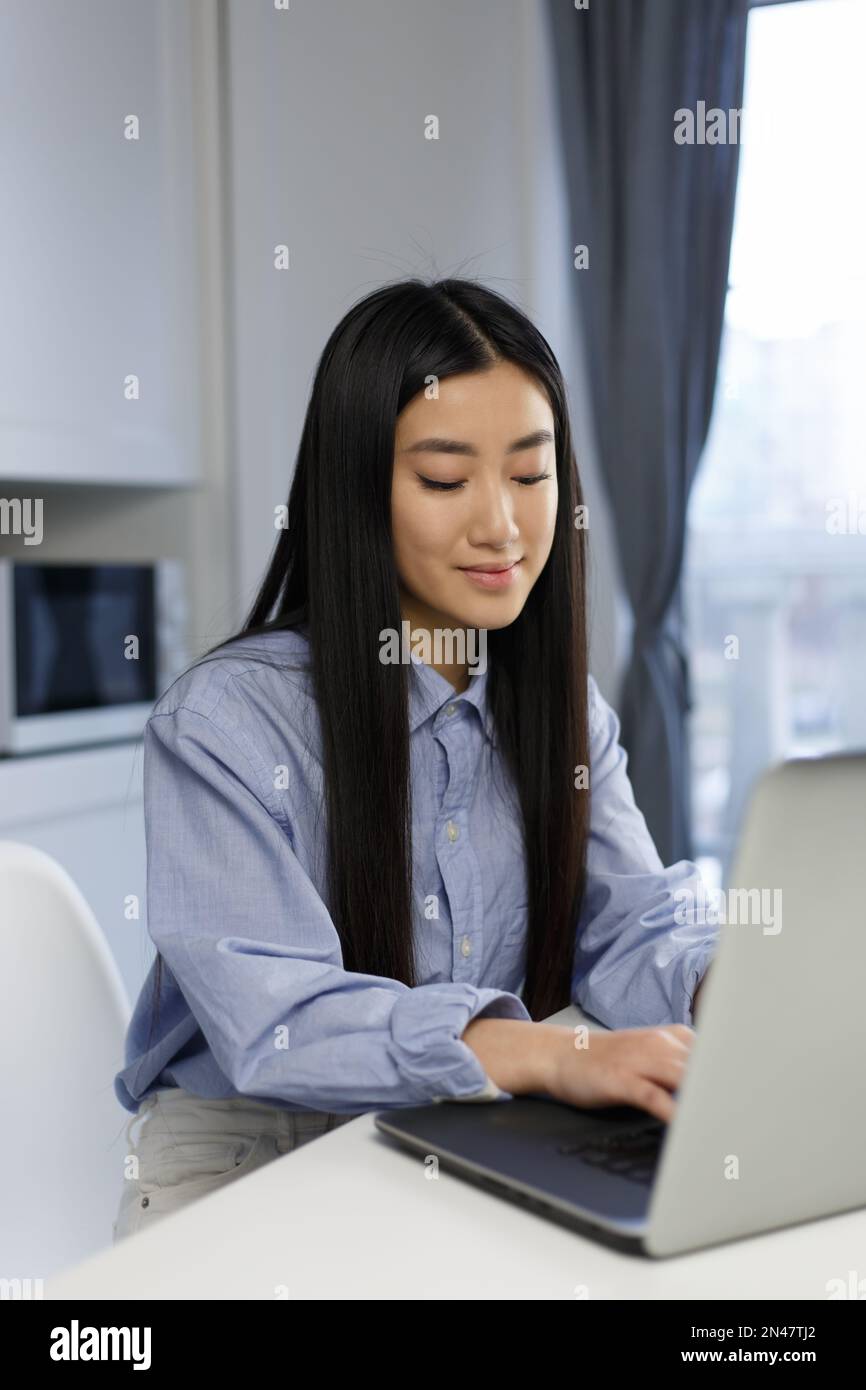 Beautiful Asian girl working on a laptop computer at home. Cheerful ...