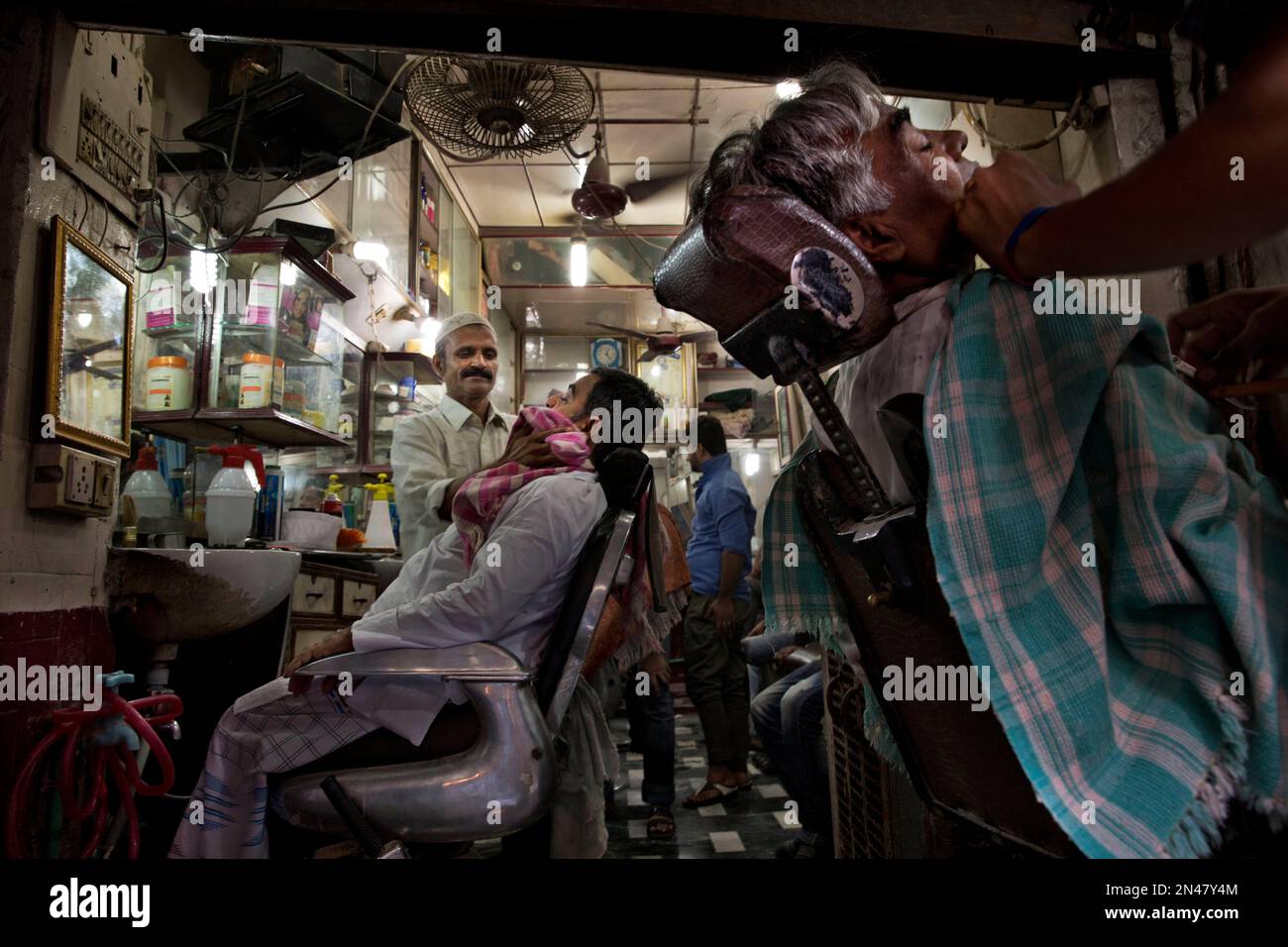 Indian barbers attend to customers at a barber shop in the old city ...