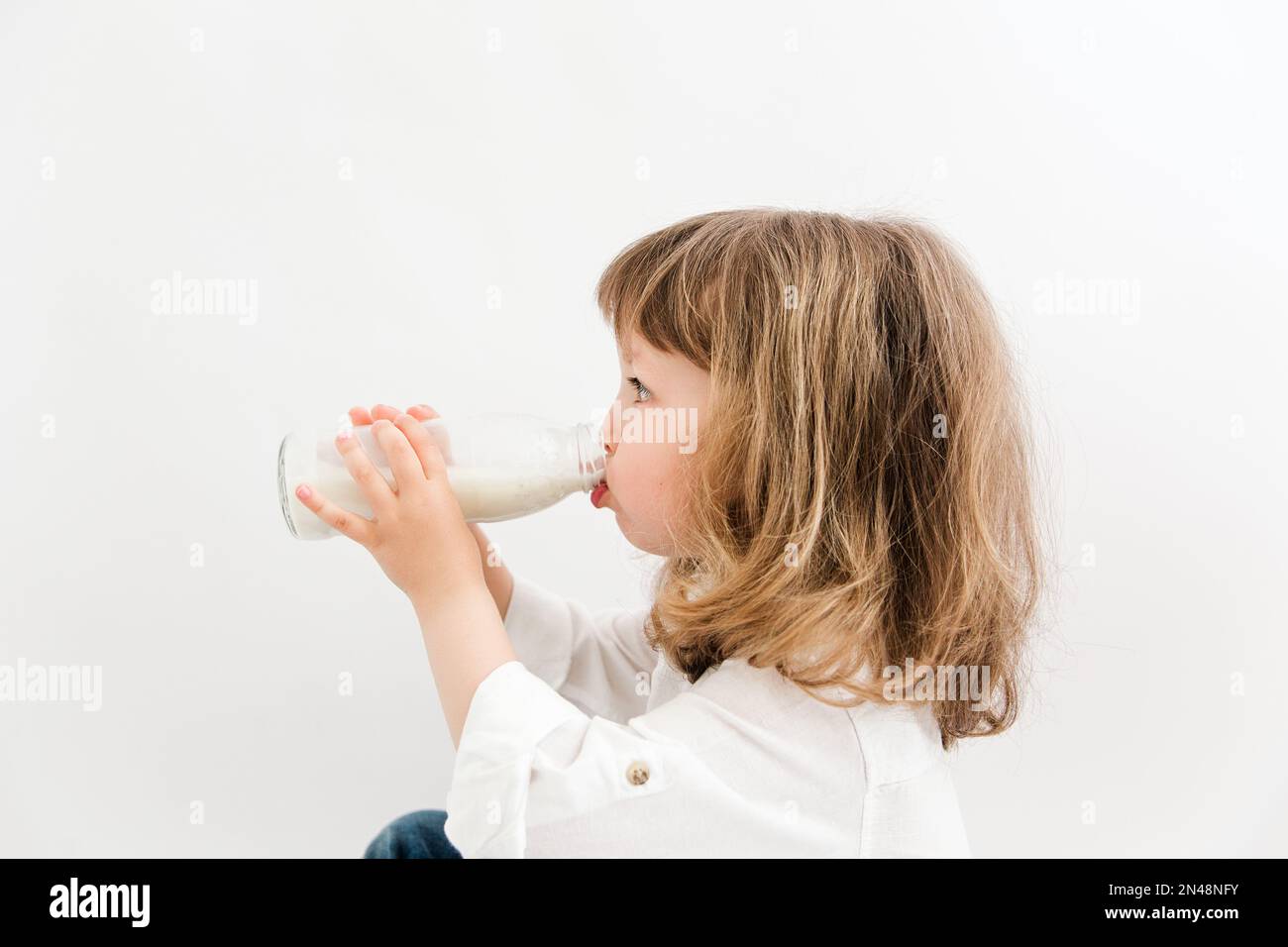 beautiful girl with curly hair and blue eyes drinks milk from a bottle ...