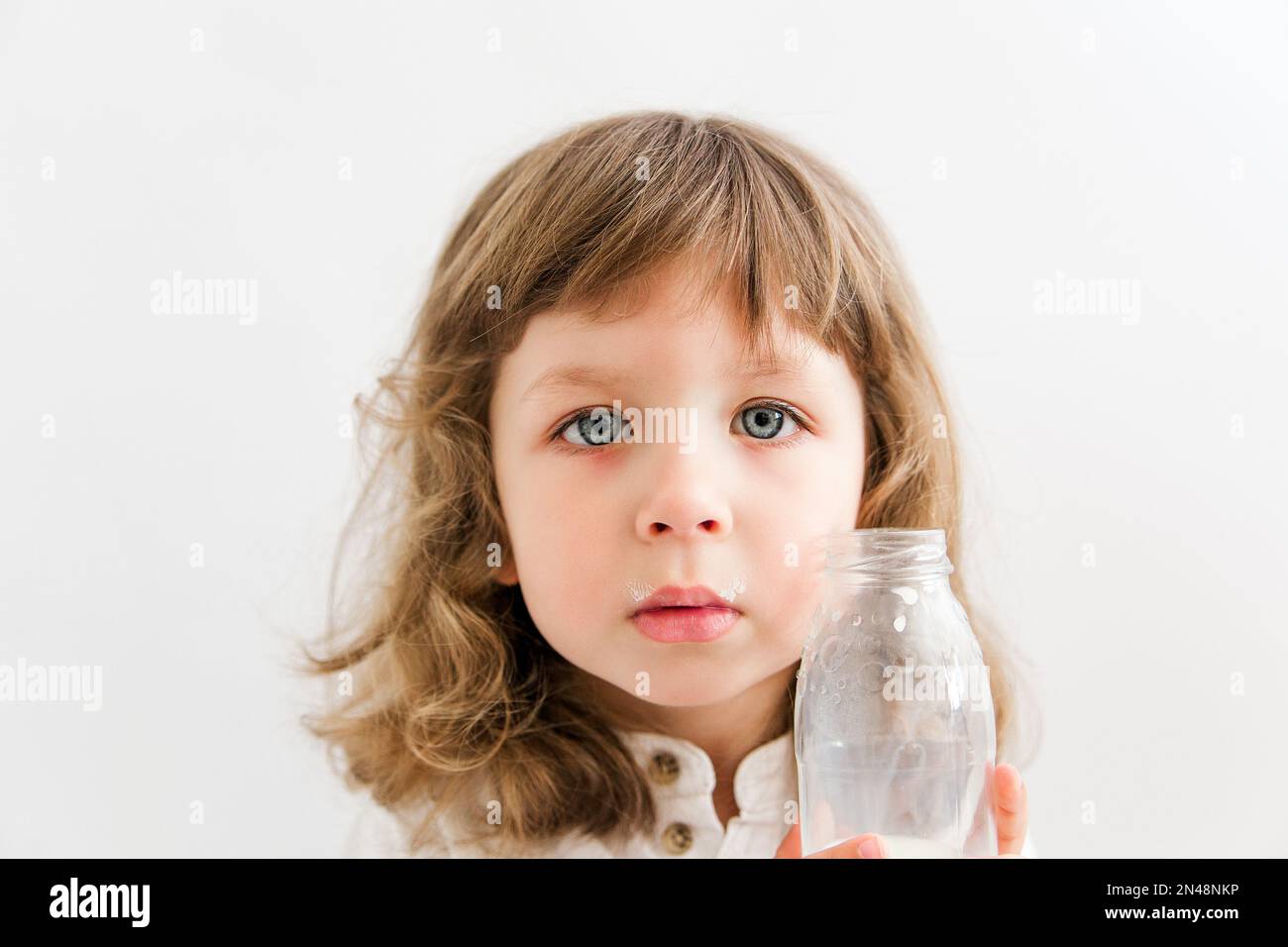 beautiful girl with curly hair and blue eyes drinks milk from a bottle. white background Stock ...