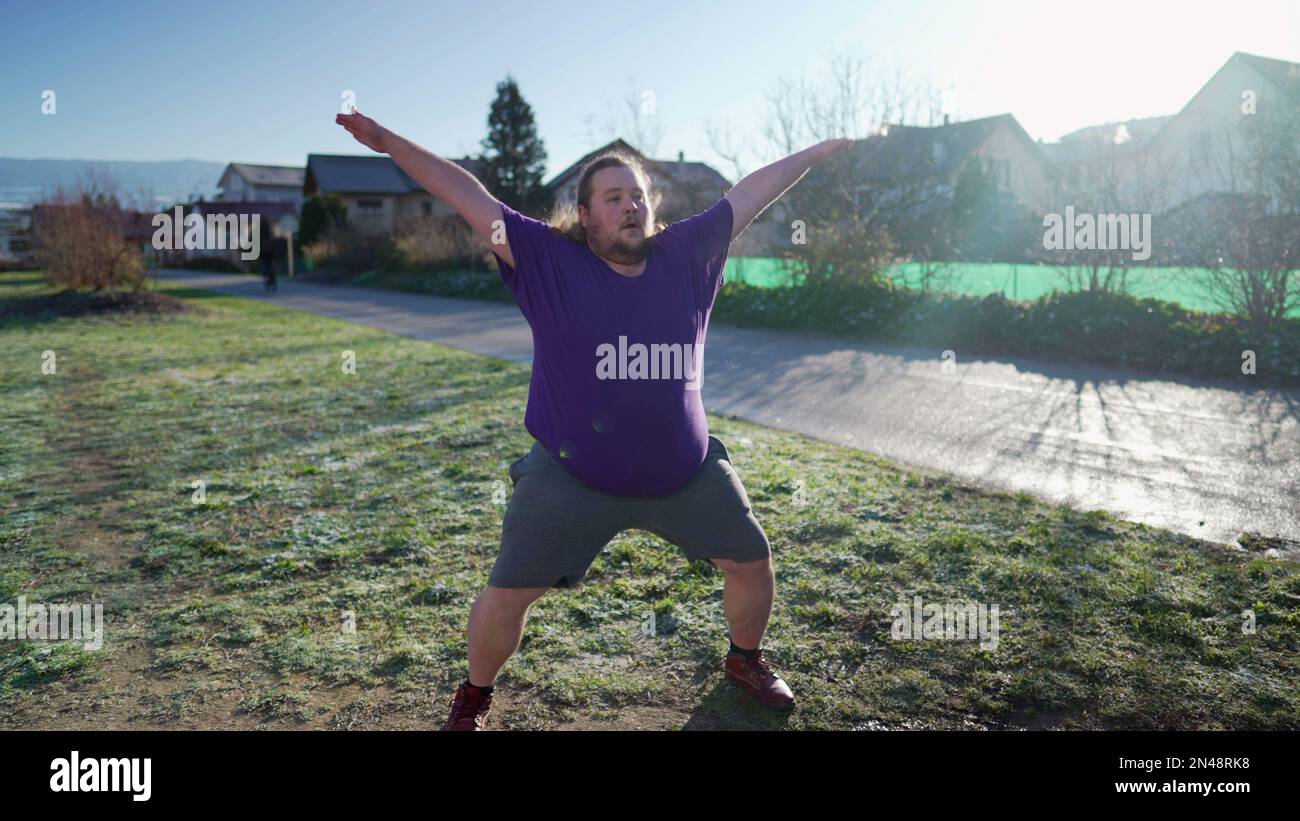 One overweight young man doing jumping jacks outdoors in the cold. Back ...