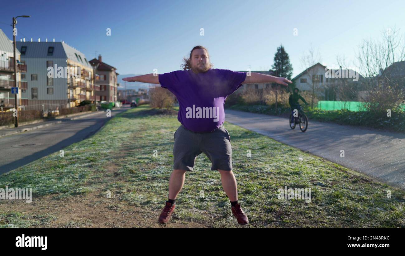One overweight young man doing jumping jacks outdoors in the cold. Back ...