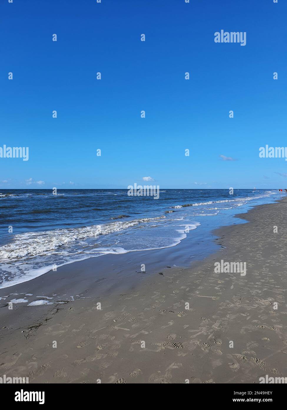 A vertical shot of the foamy waves of the North Sea hitting the sandy ...