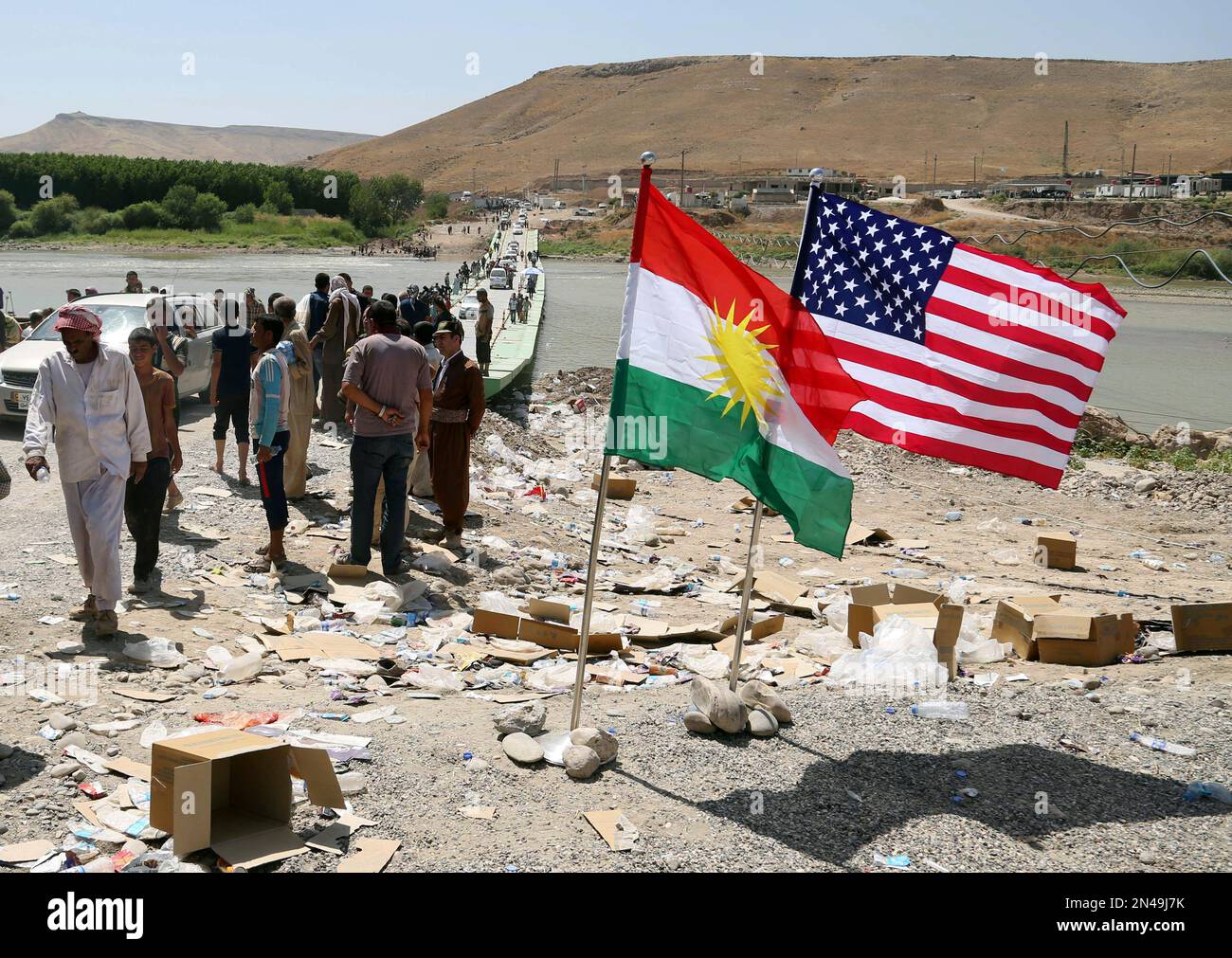U.S. and Kurdish flags flutter in the wind while displaced Iraqis from ...