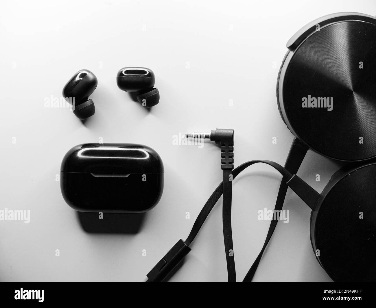 A flat lay grayscale of wireless earbuds and a headset with a wire on ...