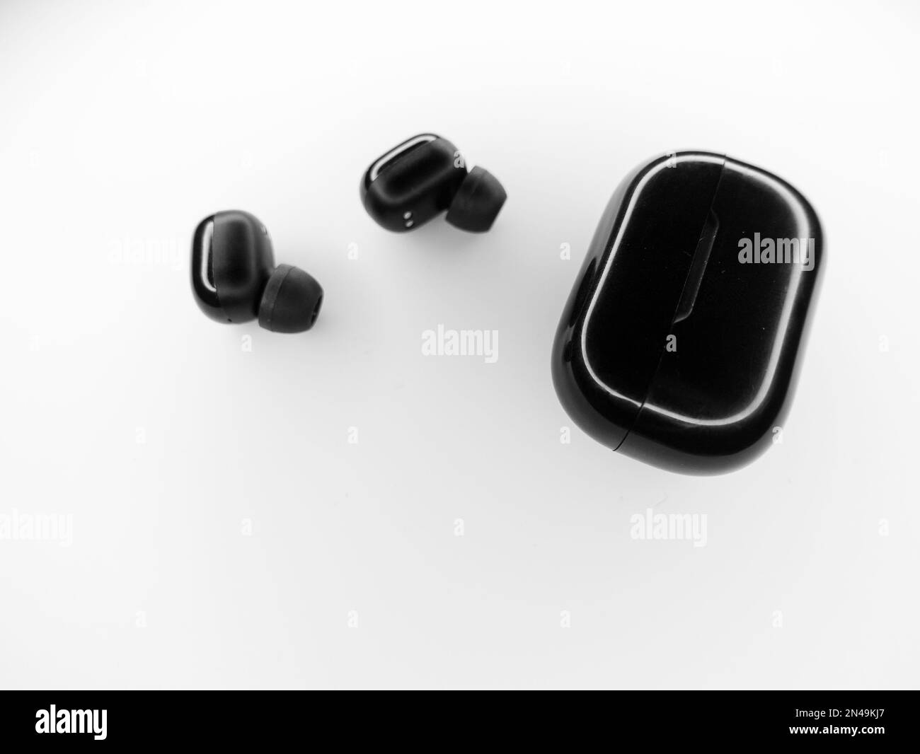 A top view grayscale of wireless earbuds and a plastic powerbank on a ...