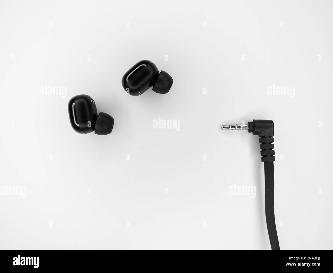 A top view grayscale of wireless earbuds and a wire of another device ...