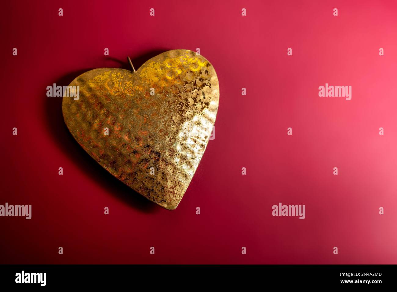 Gold colored heart shape made from metal on a red background ...