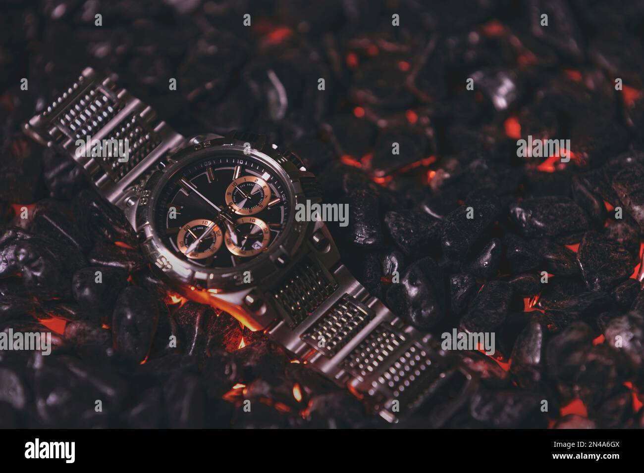 A steel watch with a black dial on black stones on an orange volcanic ...