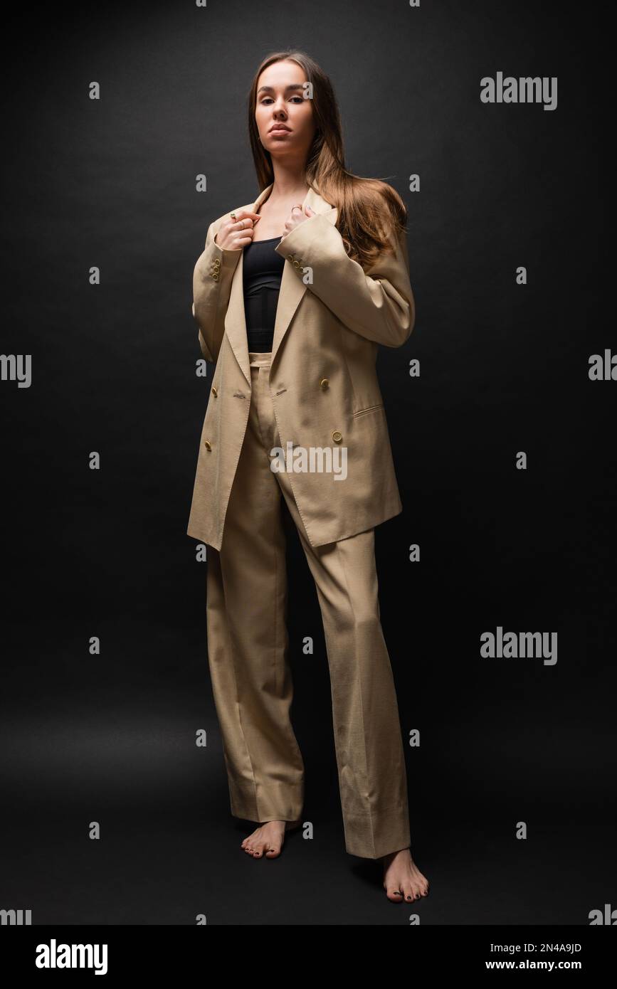 full length of barefoot woman in beige formal wear standing and looking ...