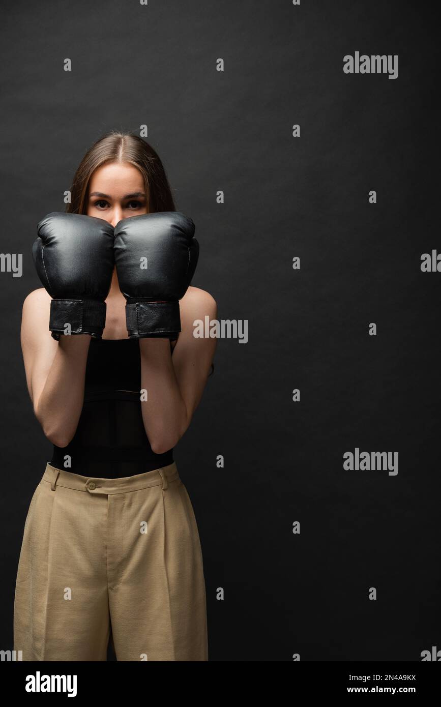 brunette and strong young woman in top covering face with boxing gloves ...