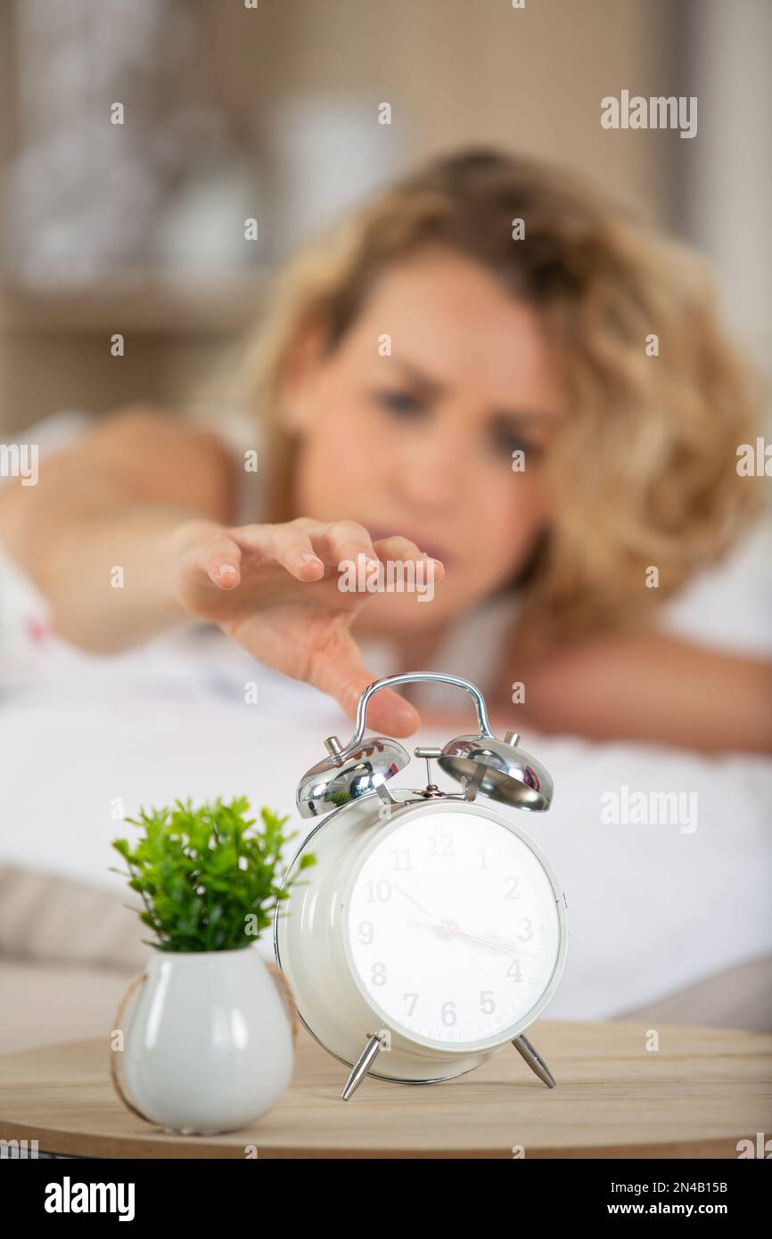 sleepy young woman reaching to stop her noisy alarm clock Stock Photo ...