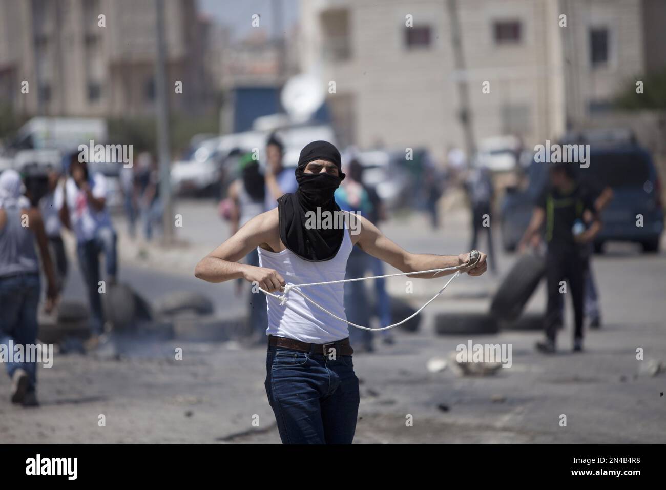A masked Palestinian uses a slingshot to hurl stones toward Israeli ...
