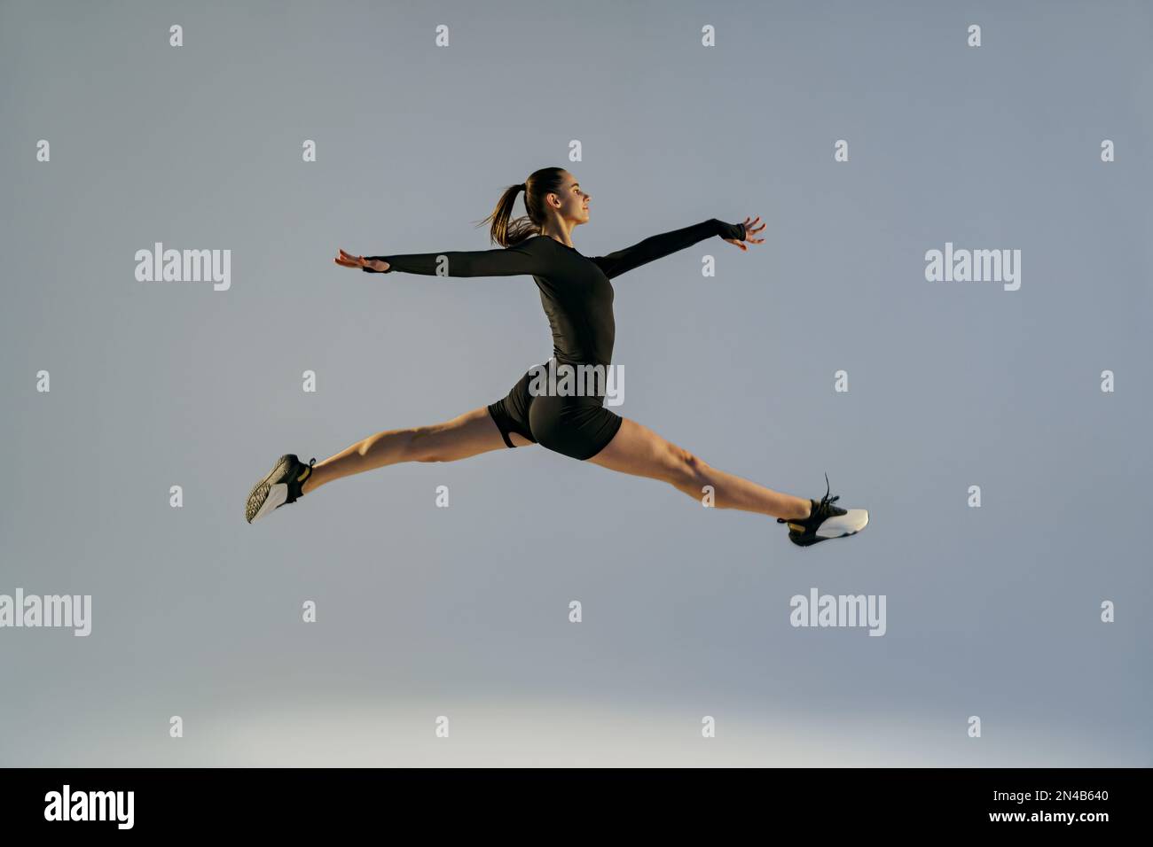 Sporty girl jumping doing split leap in air with joyful expression ...
