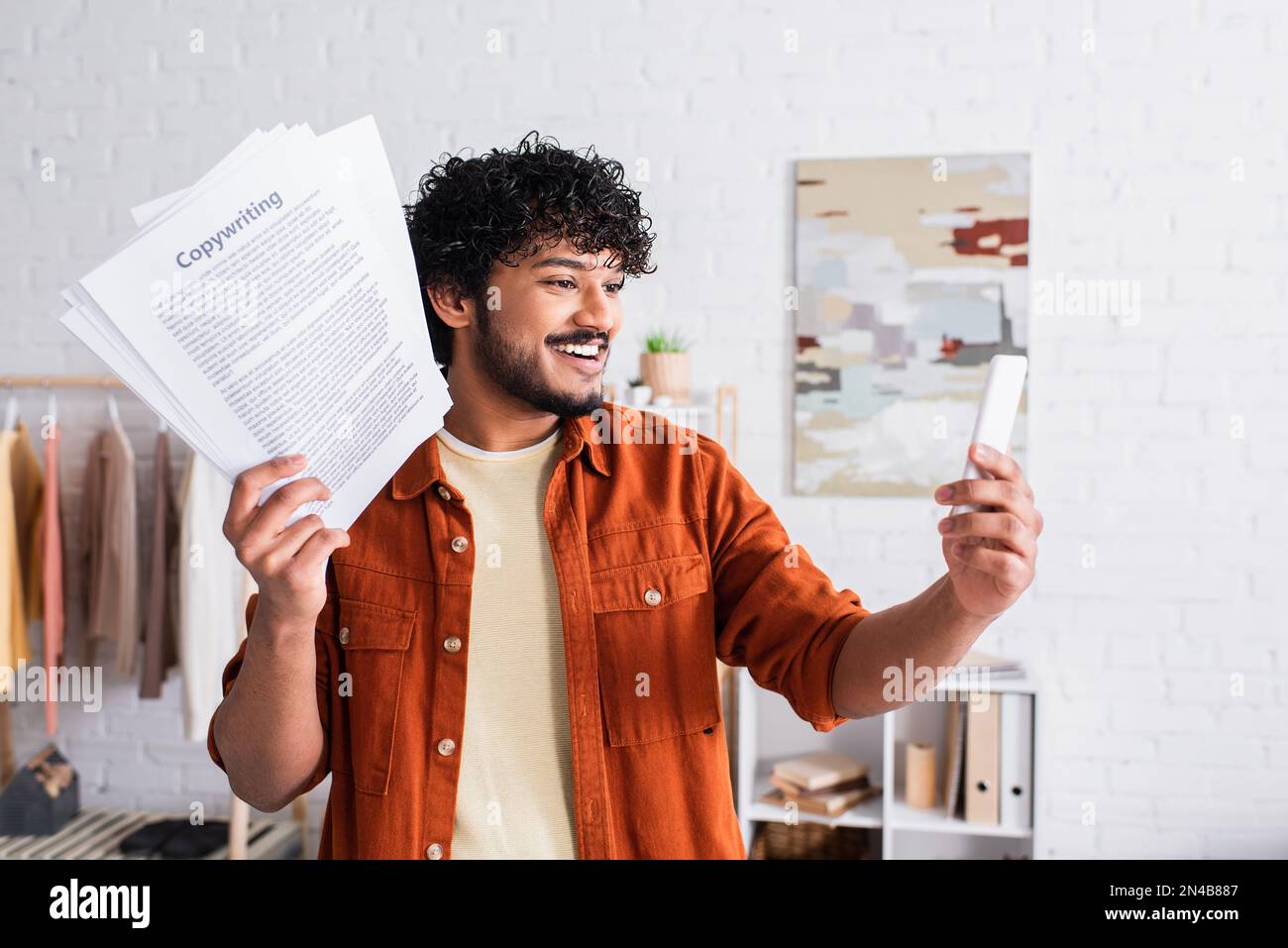 Smiling indian copywriter having video call on smartphone and holding ...