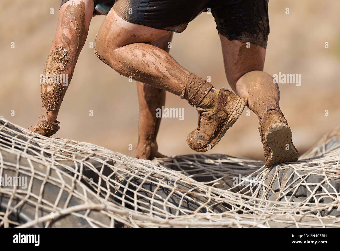 Mud race runners.The participante overcoming the obstacle made of tires Stock Photo - Alamy