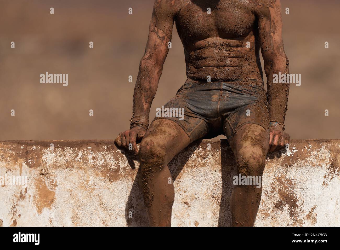 Mud race running. Running over obstacles male race participant, climbs ...