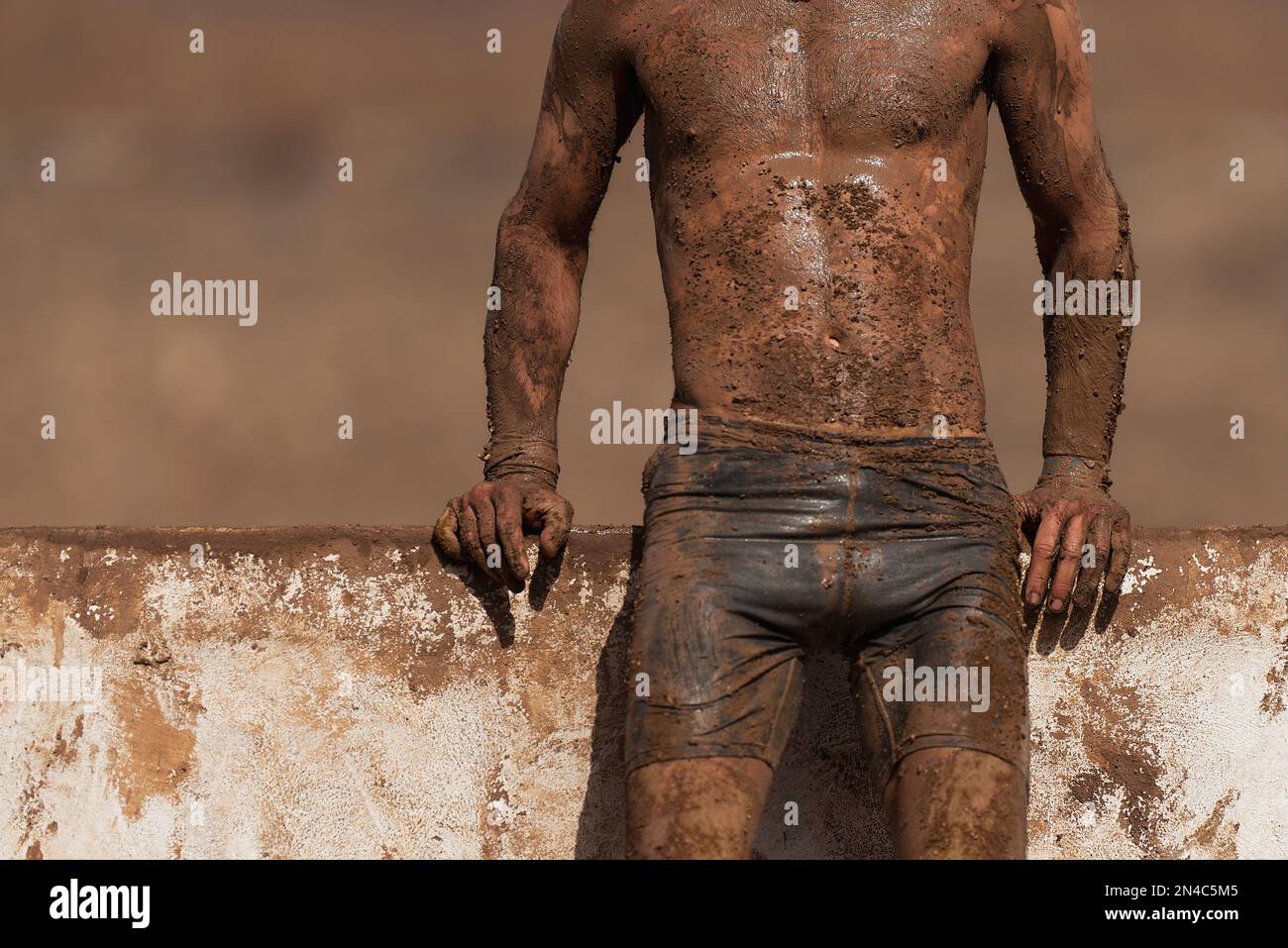 Mud race running. Running over obstacles male race participant, climbs ...