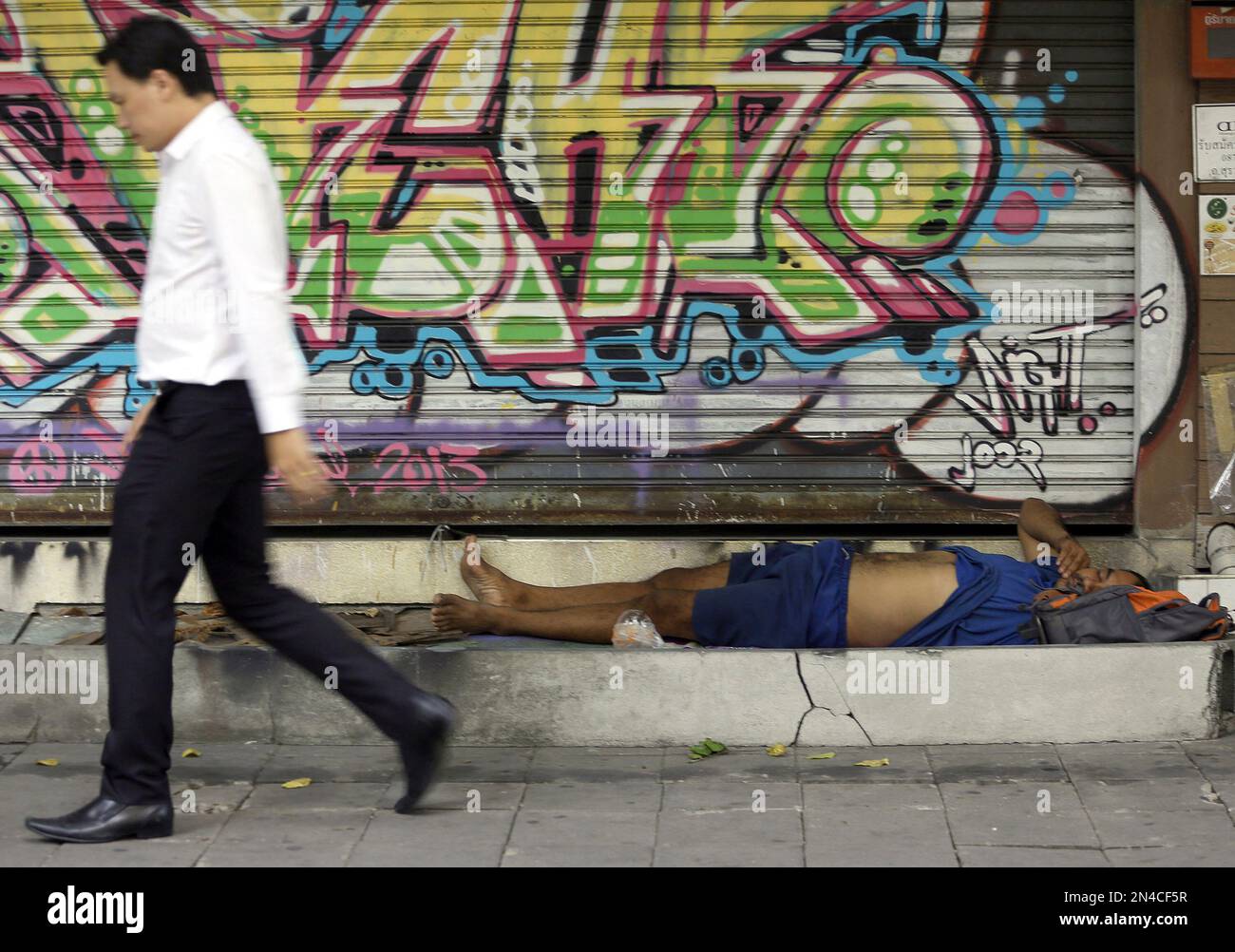 A man walks past a homeless man sleeping outside an abandoned shop in ...