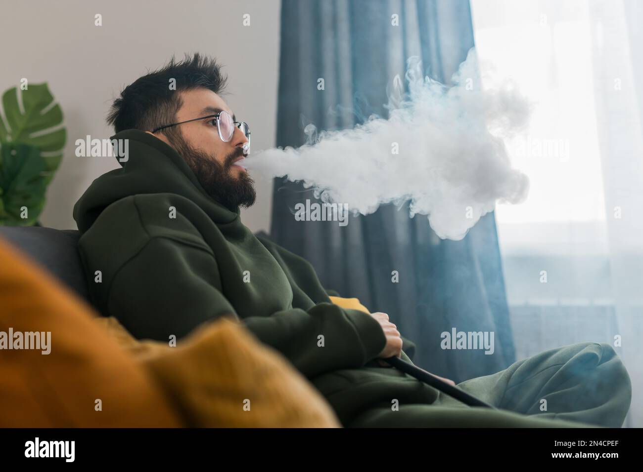 Bearded millennial or gen z man smoking hookah while relaxing on sofa ...
