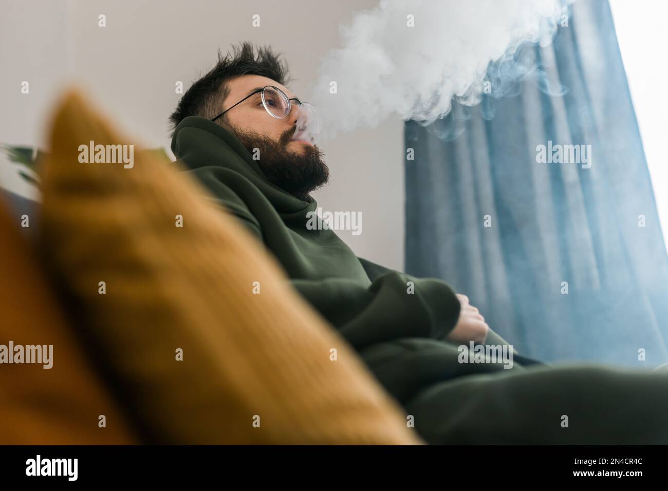 Bearded millennial or gen z man smoking hookah while relaxing on sofa ...