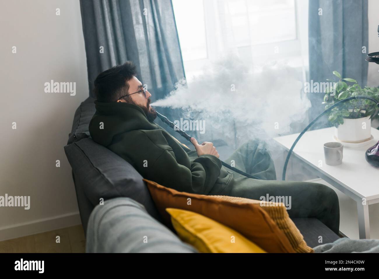 Bearded man is smoking hookah at home and blowing cloud of smoke ...