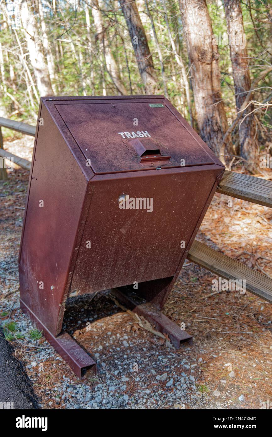 One large metal bear proof trash can in a park along a fence at a trail ...