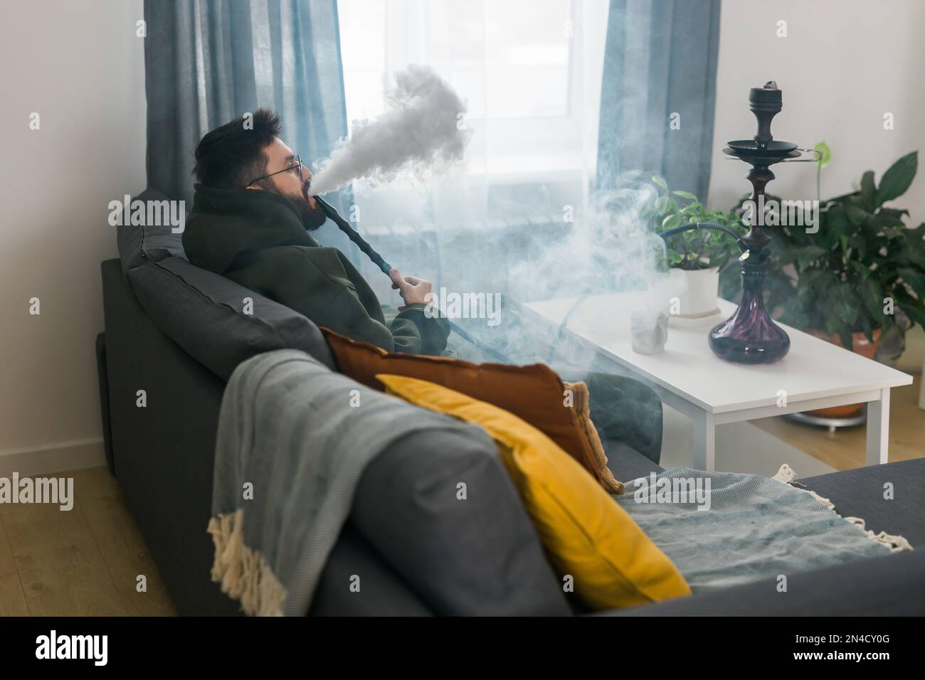Bearded man is smoking hookah at home and blowing cloud of smoke ...