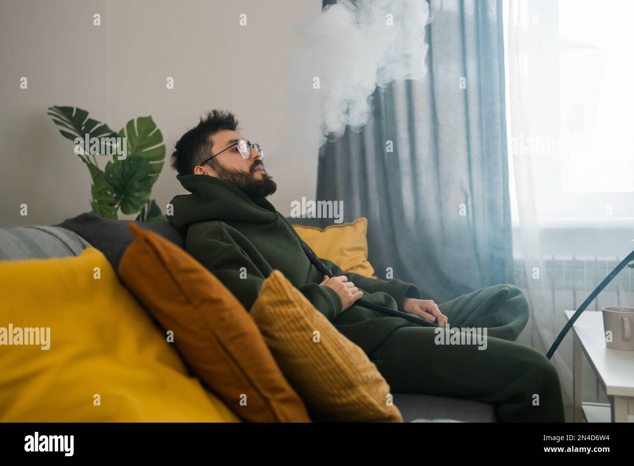 Bearded millennial or gen z man smoking hookah while relaxing on sofa ...