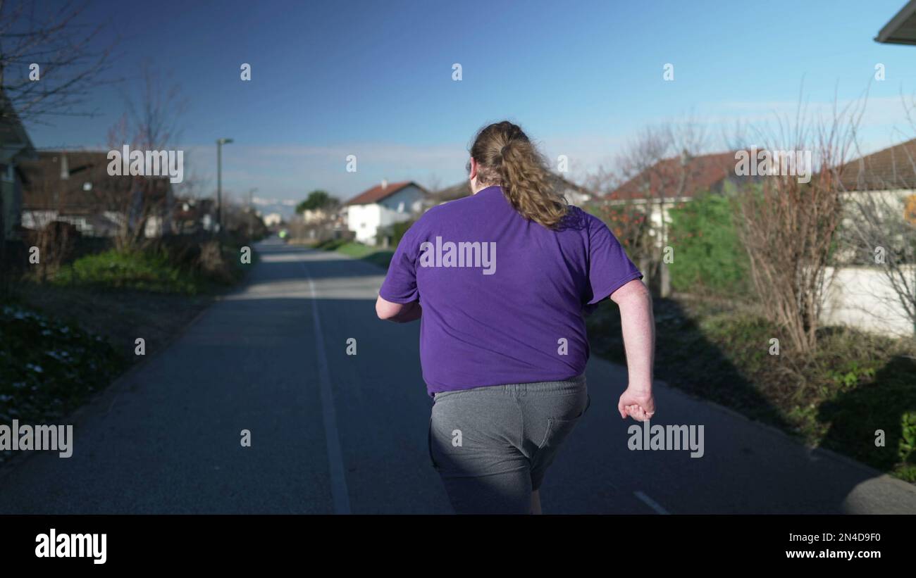 Back of one overweight man running outside in street. A fat person ...