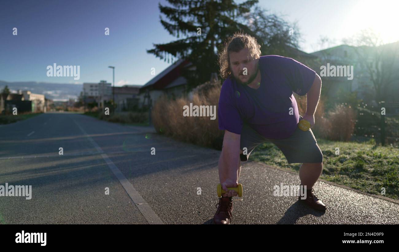 One fat man working out lifting dumbbells outside. An overweight chubby ...