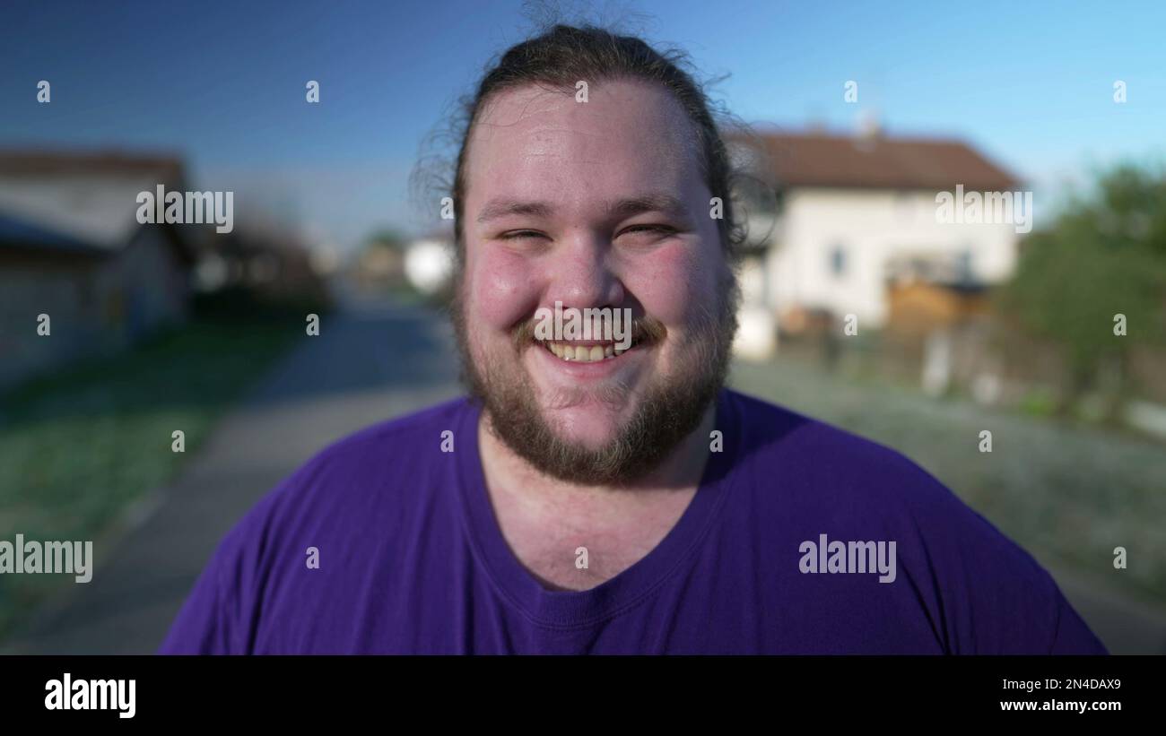 One joyful young chubby person stands outdoors smiling at camera. Overweight male person closeup ...