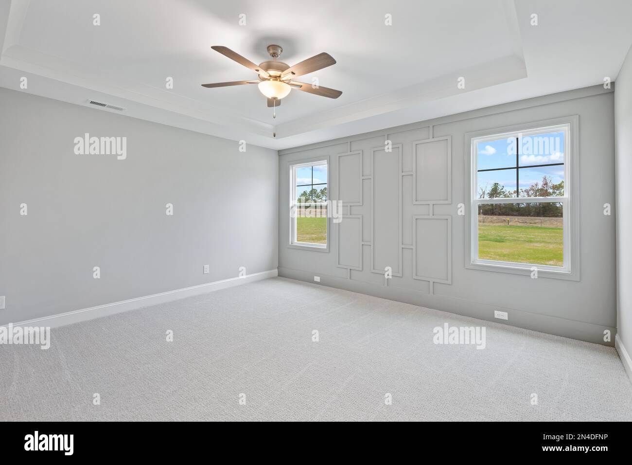 An empty master bedroom with gray walls, a ceiling fan, and windows ...