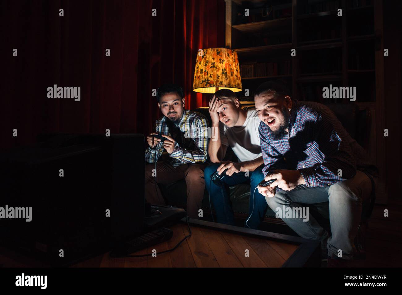 Three guys with joystick addicted to video game Stock Photo - Alamy