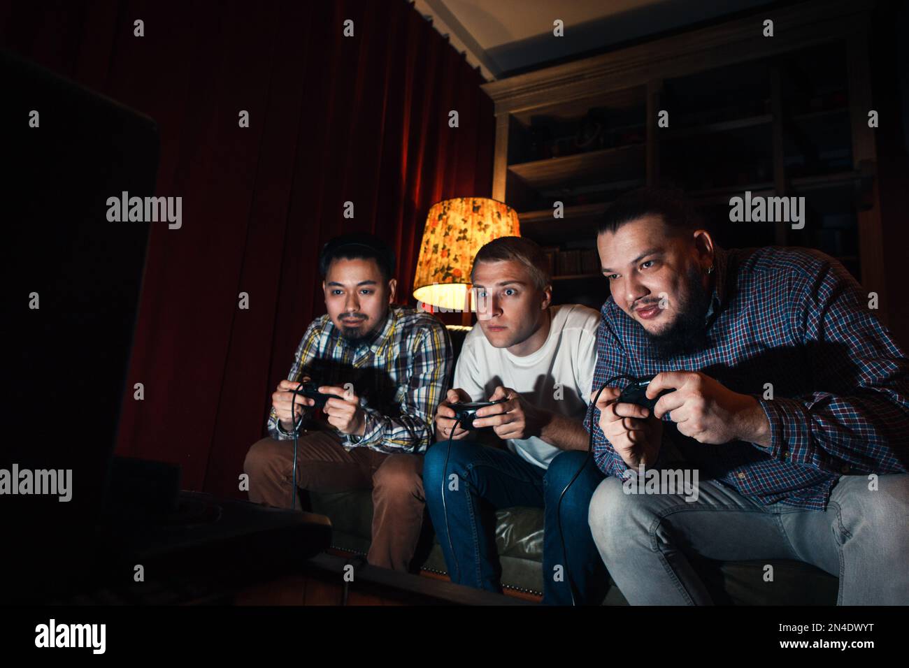Three concentrated young guy play home video game Stock Photo - Alamy