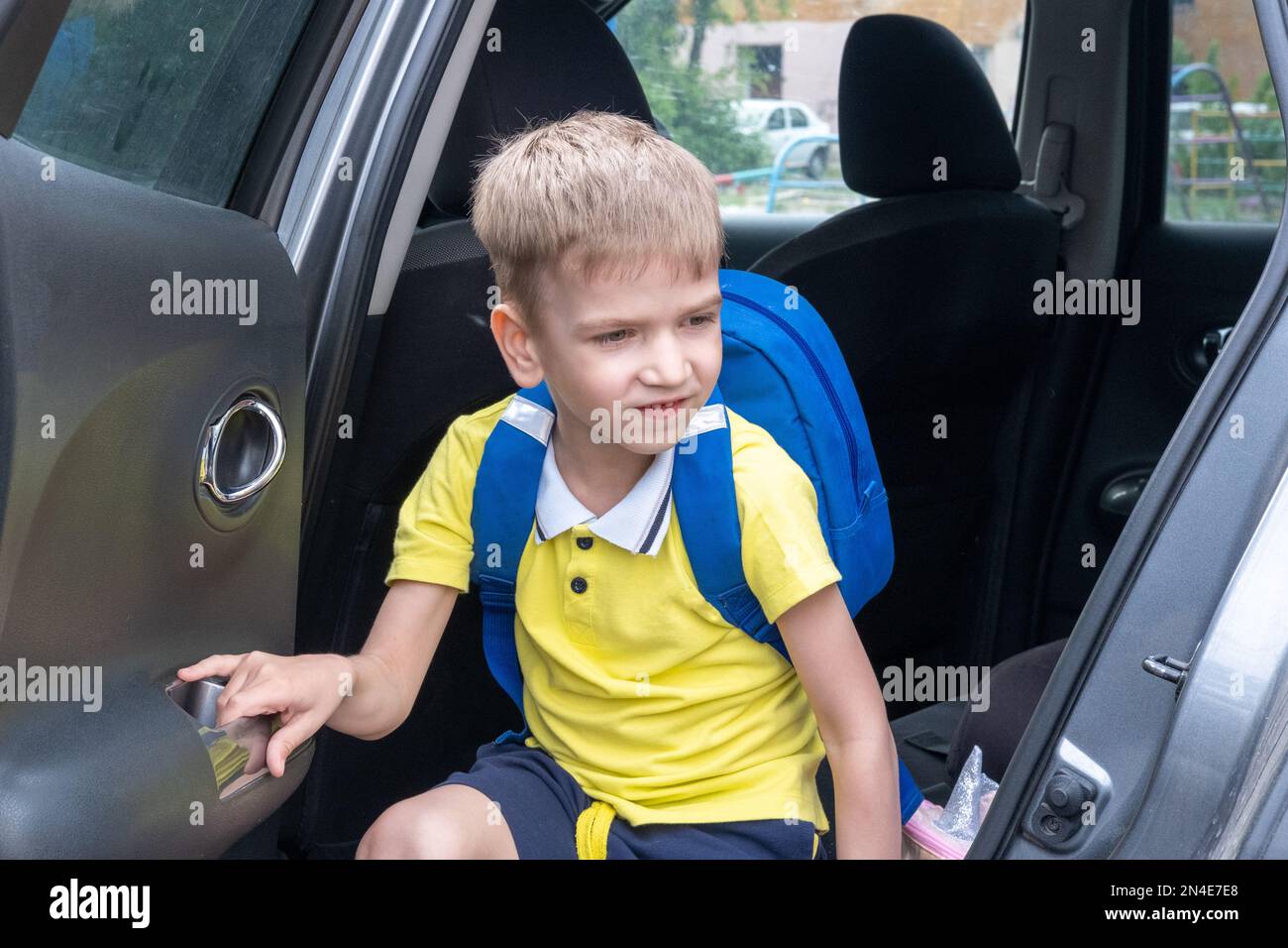 Portrait of a smiling boy with a school bag getting out of the car ...