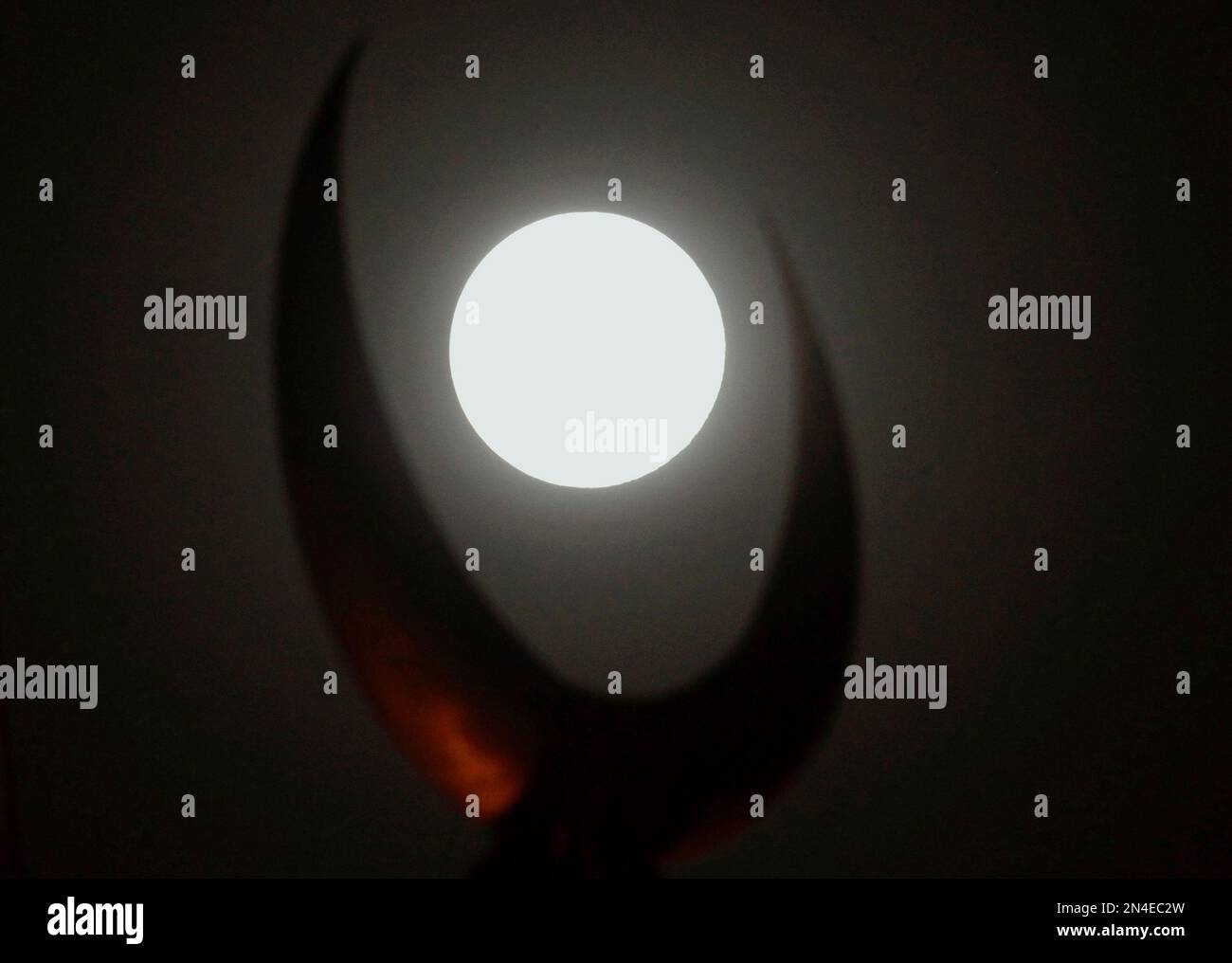 A perigee moon, also known as a supermoon, looks through a crescent of ...