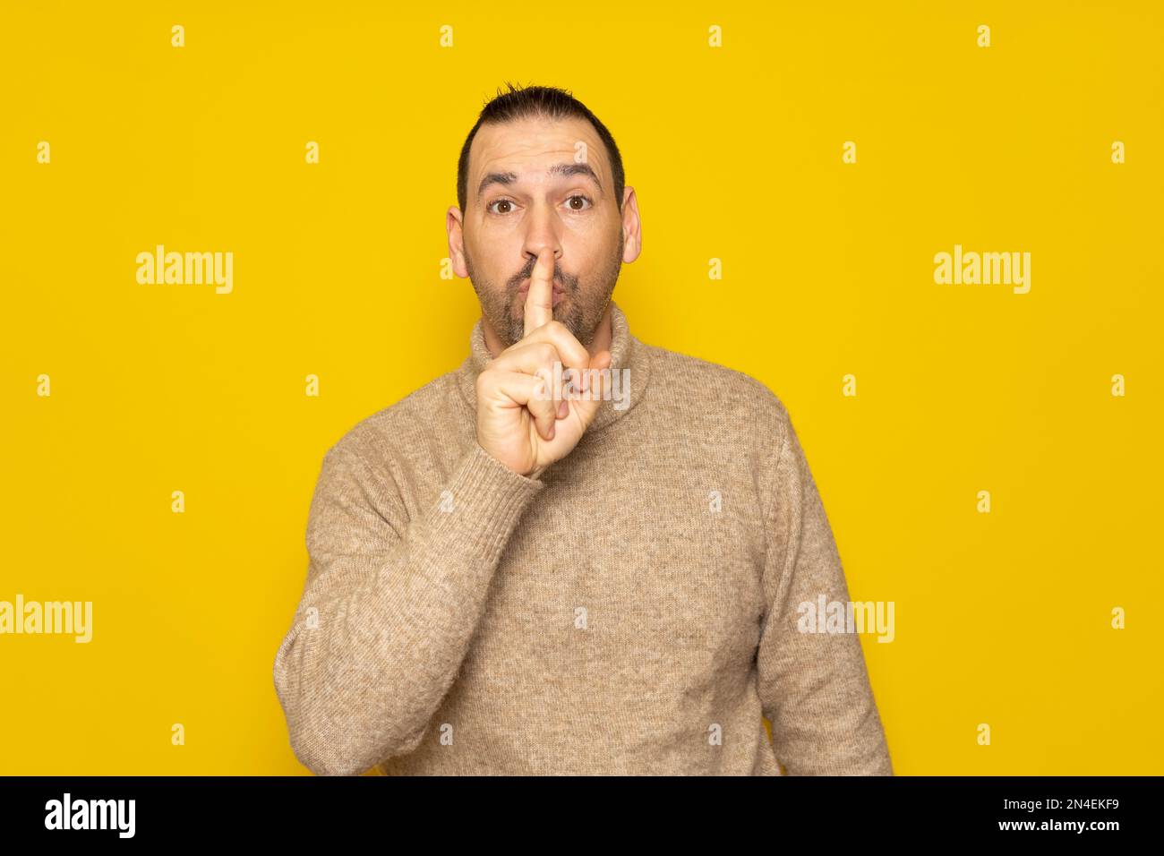 Serious handsome man puts his index finger to his lips, tries to keep ...