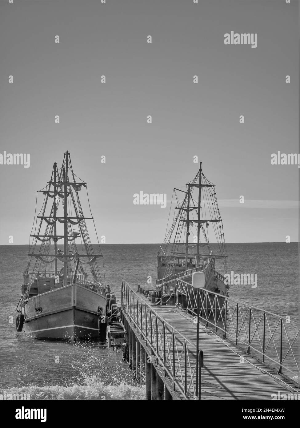 Two wooden sailing ships at the wooden pier against the sea. BW photo ...