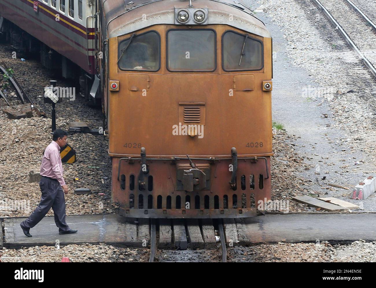 A man walks on a path past a backwards running train in Bangkok ...
