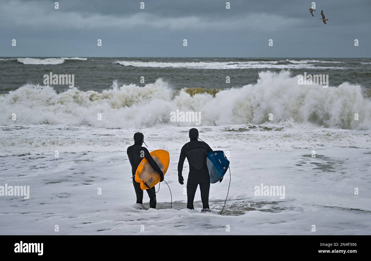 29 January 2023, Denmark, Vorupör: Surfers stand in the waves of the ...
