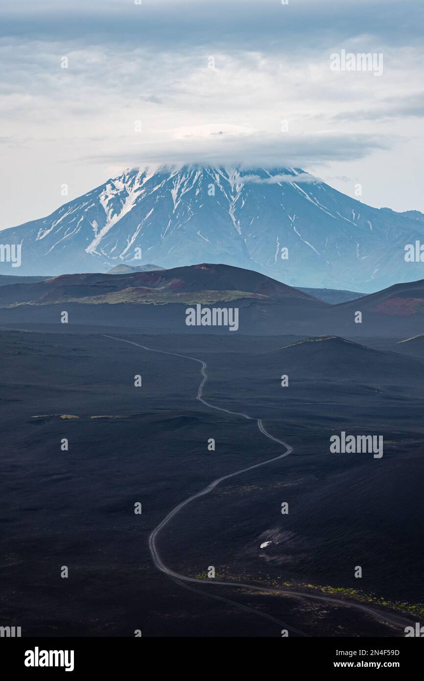 Road to volcano, snowy mountain through dark lava-covered ground and ...