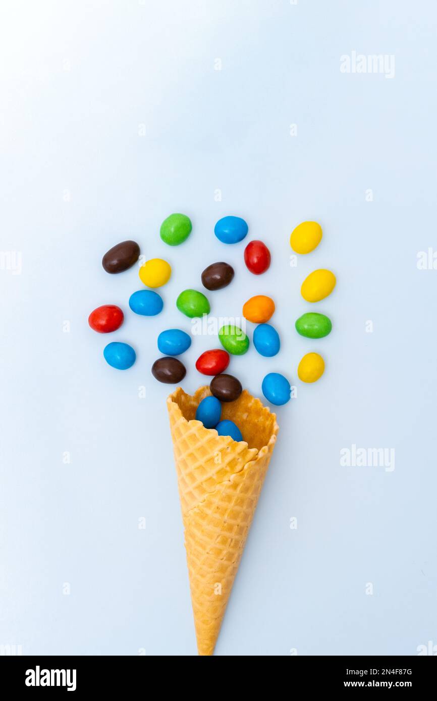 A conical empty waffle cone and scattered multicolored round candies ...