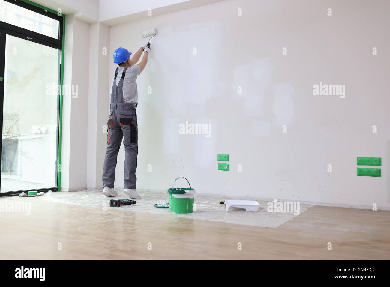 Decorator in hard hat paints apartment wall with roller brush Stock ...