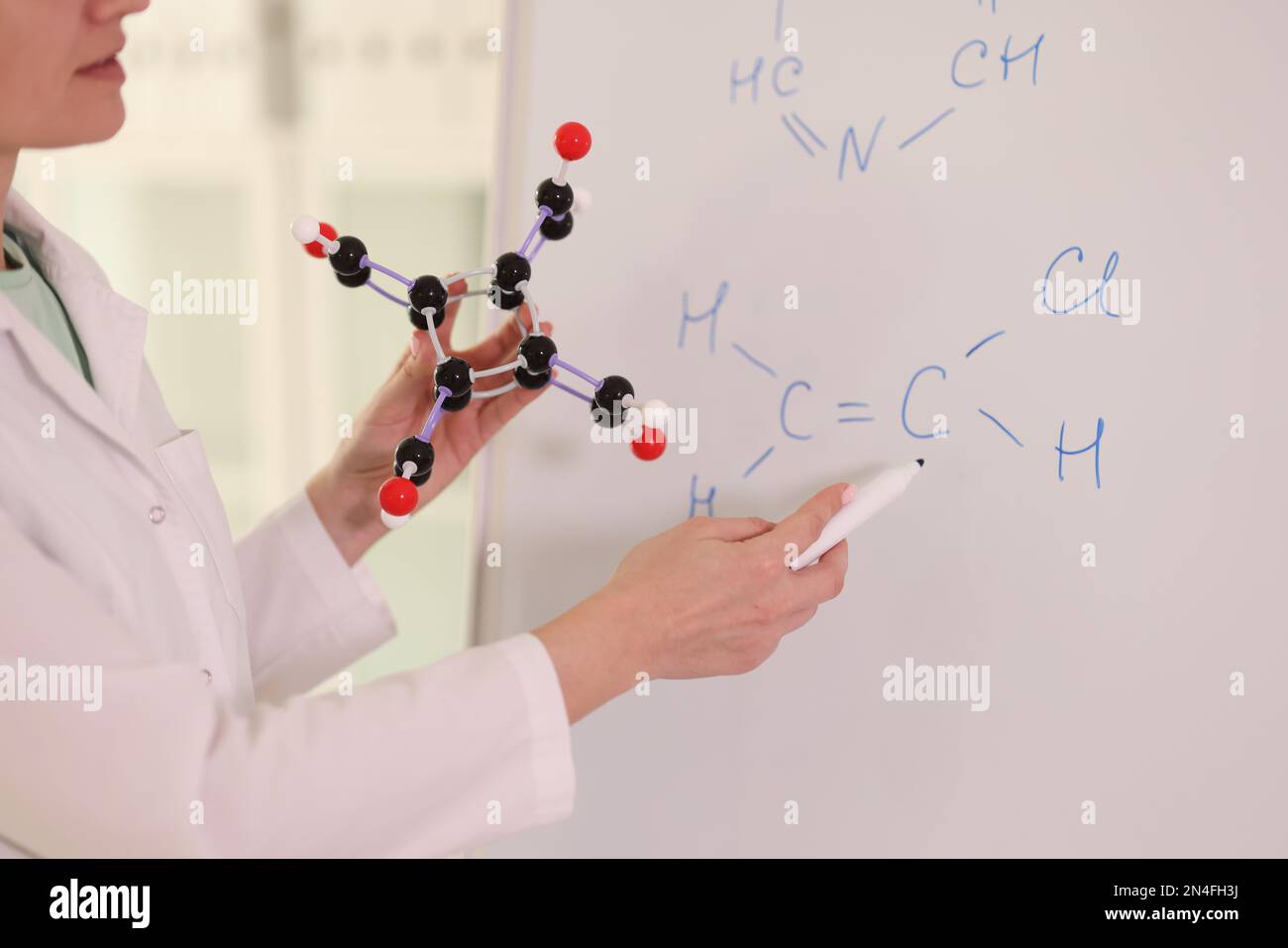 Female chemist holding molecular model and drawing chemical formulas on ...
