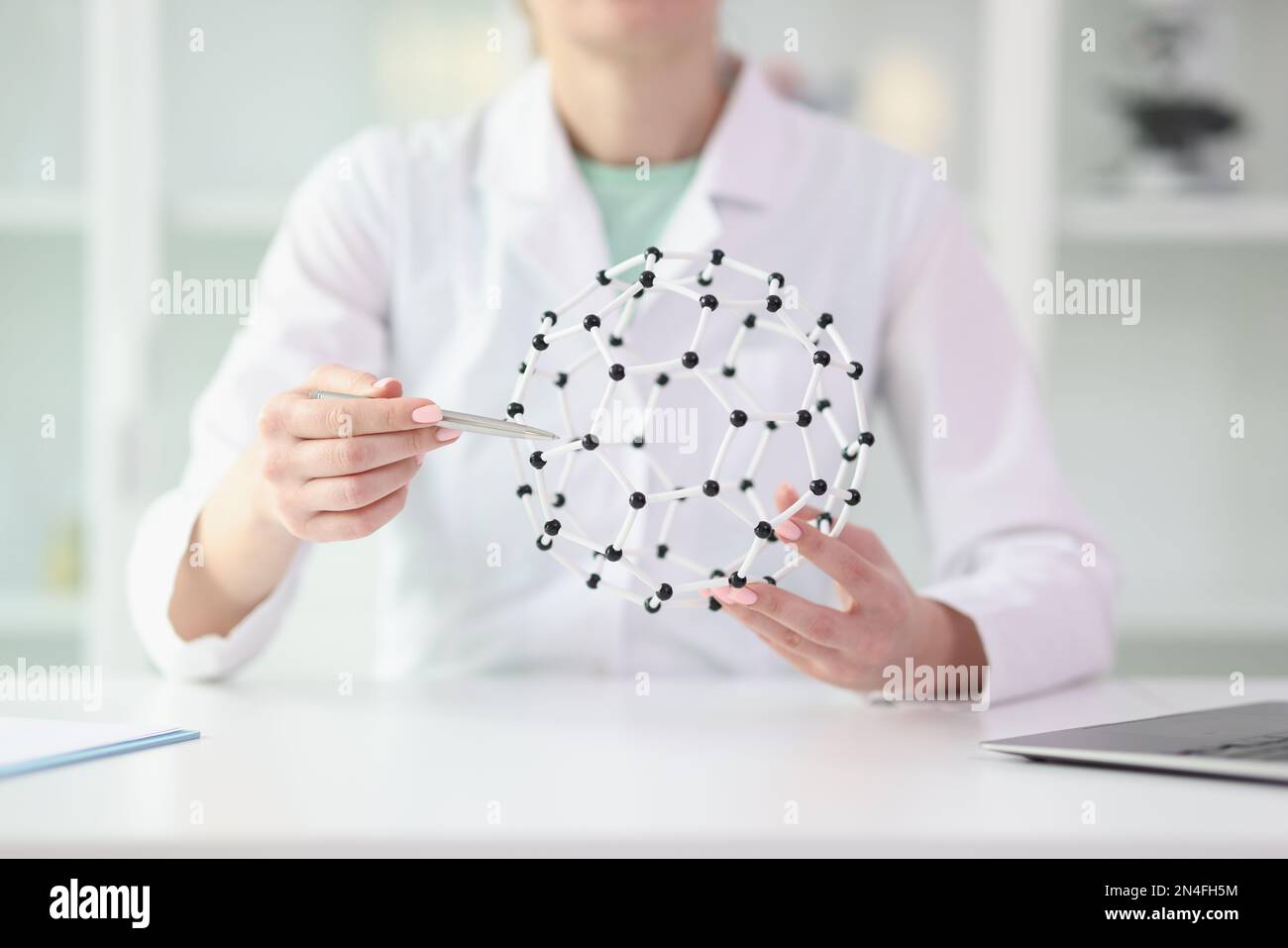Woman scientist shows model of molecular structure in her hands, sitting at laboratory table ...