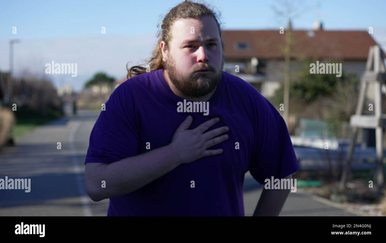 One exhausted overweight young man having chest pains standing outside ...
