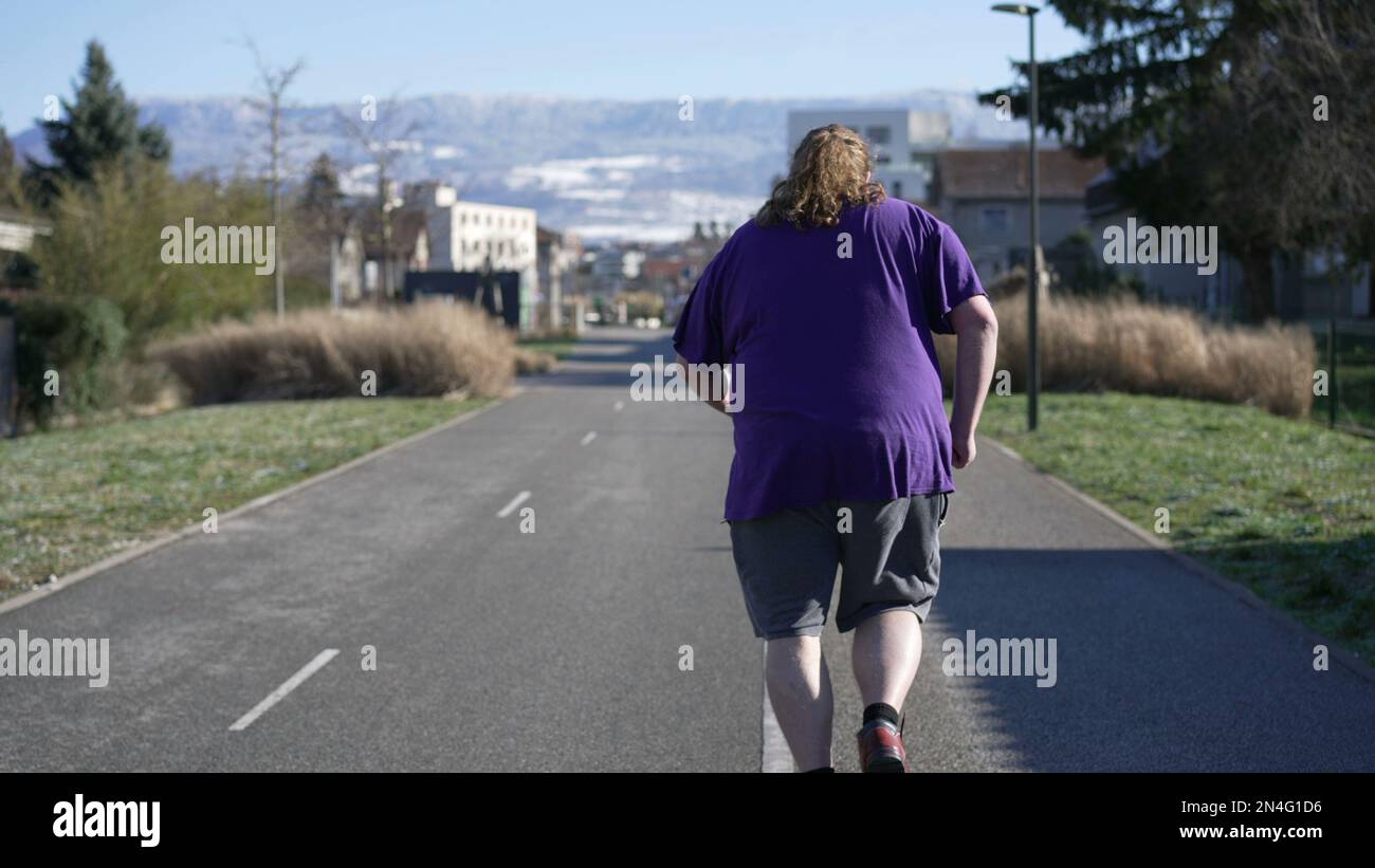 Back of One young overweight man jogging outdoors. Tracking shot of a ...