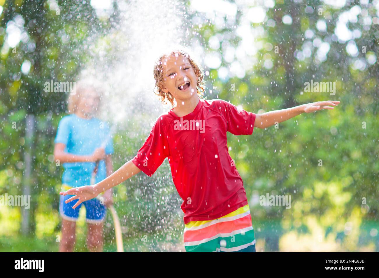 Kids play with water sprinkle hose. Summer garden outdoor fun for ...